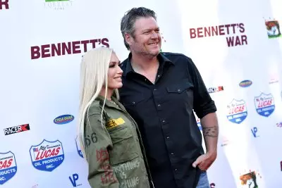 Gwen Stefani w zielonej wojskowej kurtce stoi z Blake Shelton w czarnym guziku na czerwonym dywanie Bennetts War