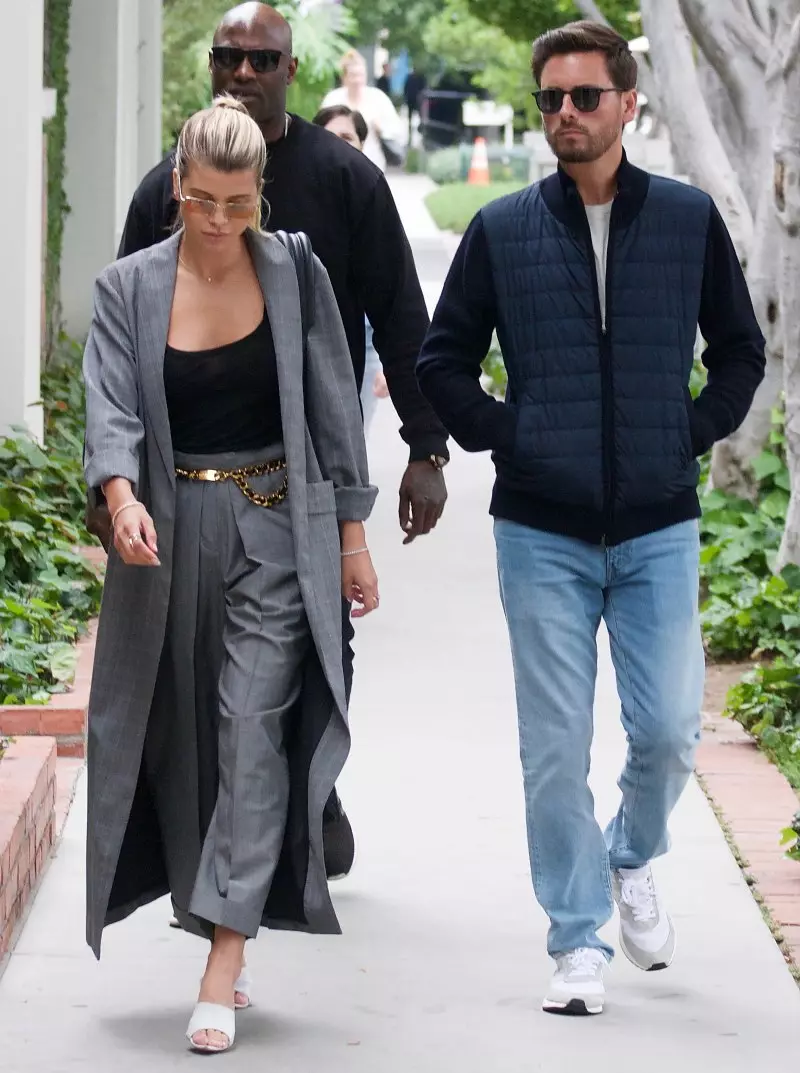 Sofia Richie Akuyenda Ovala Bulu Lovala Buluu Wakuda Tank Top ndi Coat Wautali Wabuluu Wokhala Ndi Magalasi Adzuwa Pamene Akuyenda WIth Boyfriend Scott Disick atavala Blue Jeans Blue Jacket and Sunglasses