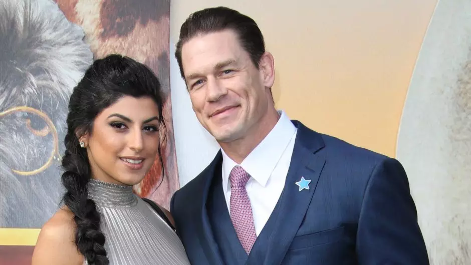 John Cena na Blue Suit na Pink Tie na enyi nwanyị Shay Shariatzadeh na Shimmery Silver Dress na Ogologo Braid Smile na Kapeeti Uhie.