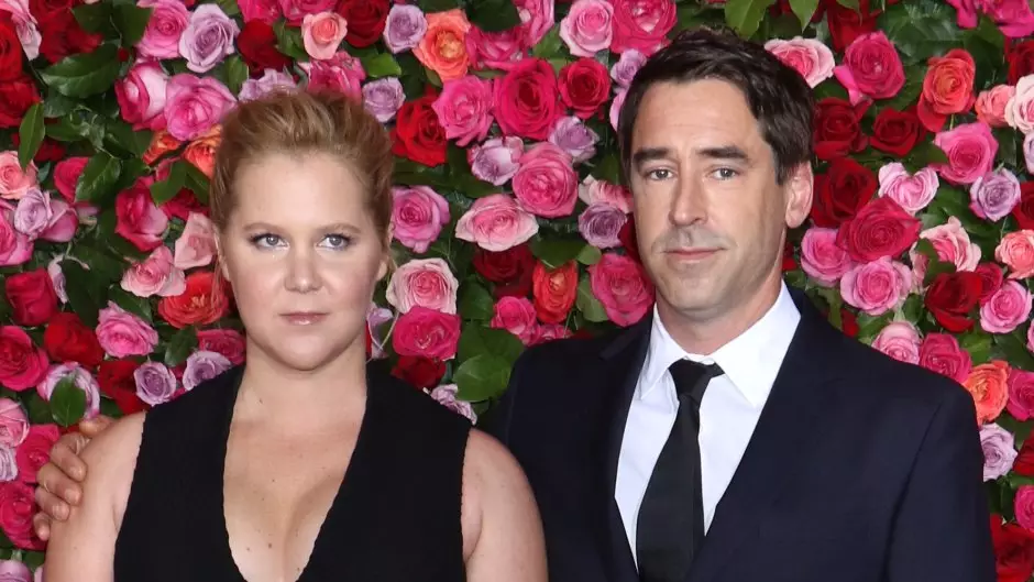 Amy Schumer nganggo Gaun Ireng lan Bojone Chris Fischer nganggo Setelan Biru Ngadeg ing Karpet Abang Bareng