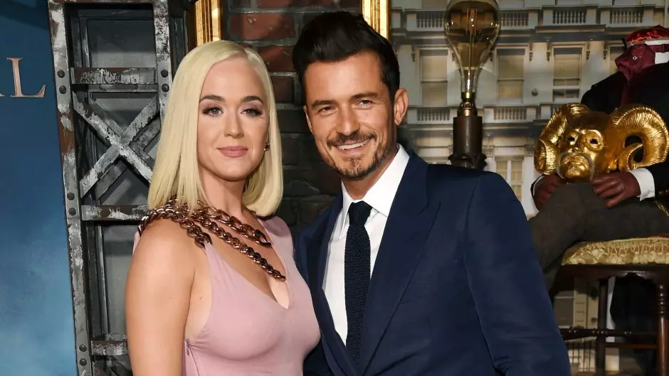 Katy Perry sorrí cun vestido rosa con cadeas e un bob louro co prometido Orlando Bloom en traxe azul