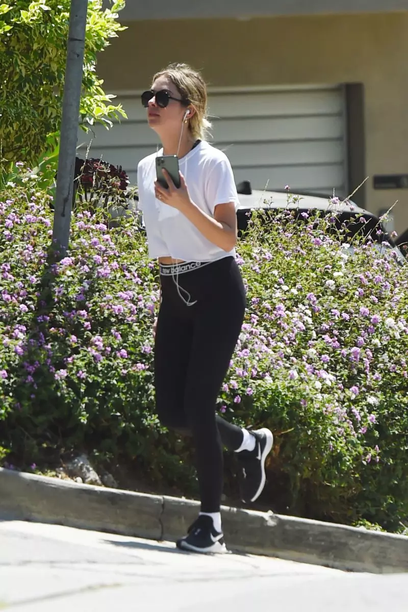 Lîstikvan Ashley Benson dema ku li Los Angelesê dimeşe û bi têlefonê diaxive tshirt spî û pantolonên reş û tavê li xwe dike.