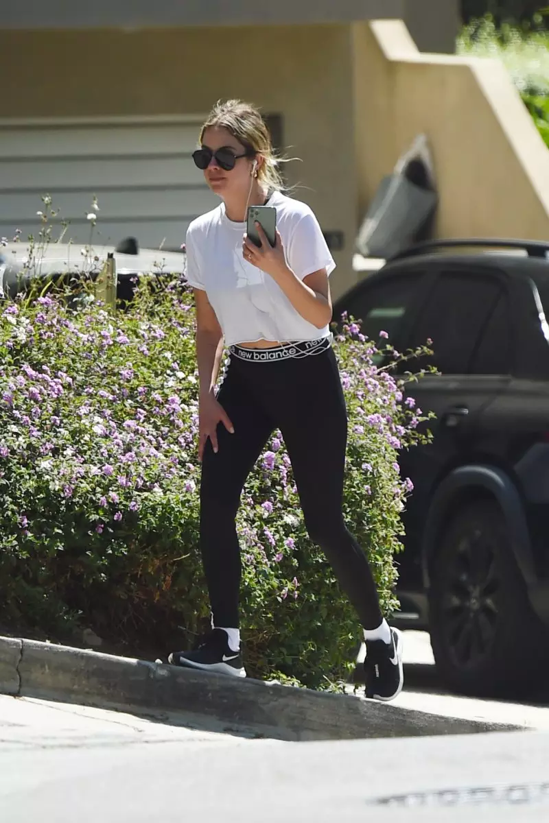 Atriz Ashley Benson usa camiseta branca e calça preta e óculos de sol enquanto caminhava em Los Angeles falando ao telefone com tênis preto em meio a Cara Delevingne Split