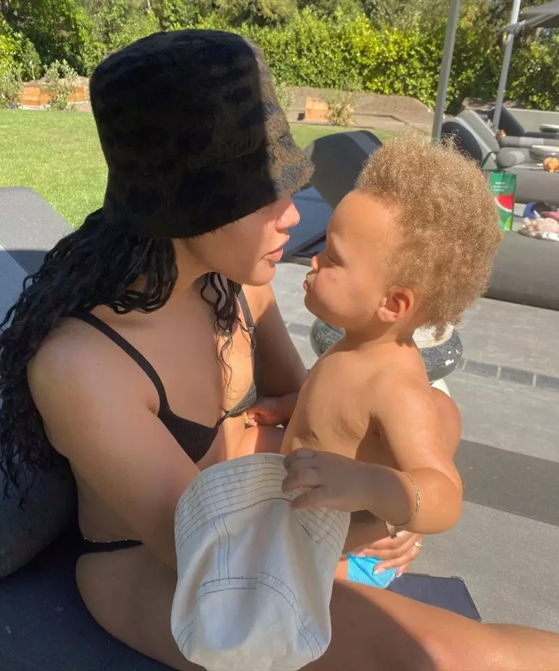 Ayesha Curry y su hijo Canon se sientan junto a la piscina Ayesha usa sombrero de pescador y bikini negro