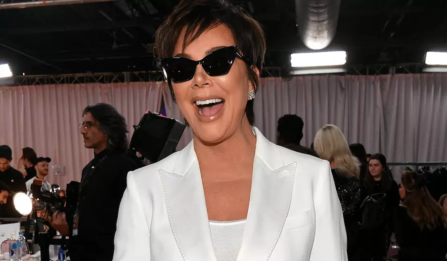 Kris Jenner seuri bari maké kacamata hideung jeung jas calana bodas