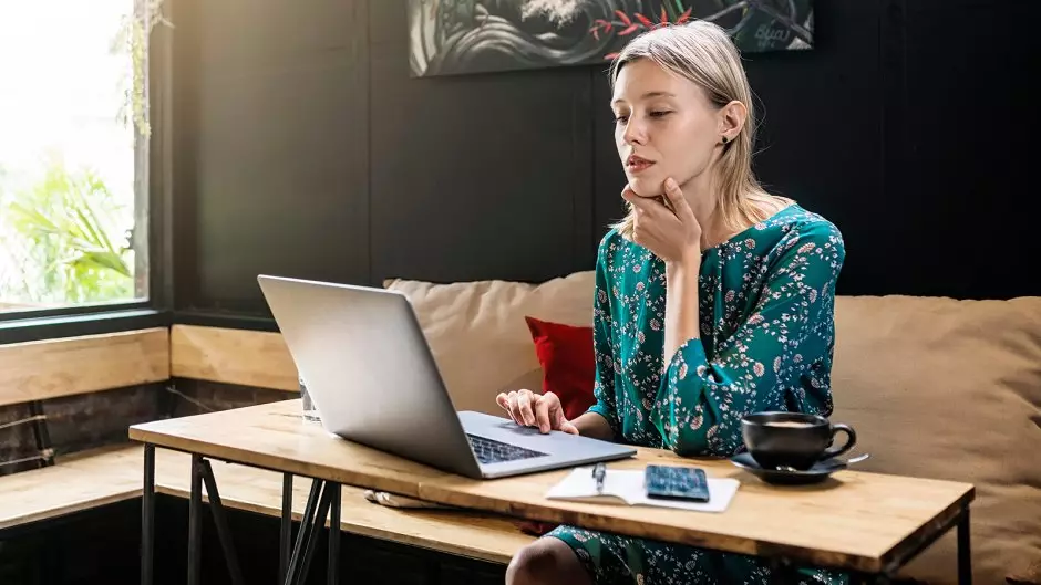 אישה צעירה עם שמלה ירוקה יושבת בבית קפה ועובדת על המחשב הנייד שלה