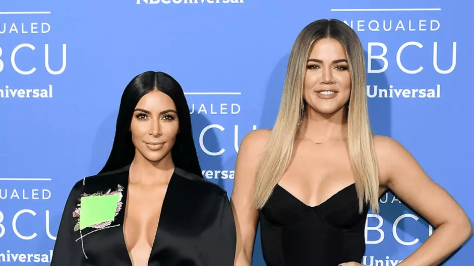 Kim Kardashian eta Khloe Kardashian beltzez jantzita atzealde urdin baten aurrean posatzen.