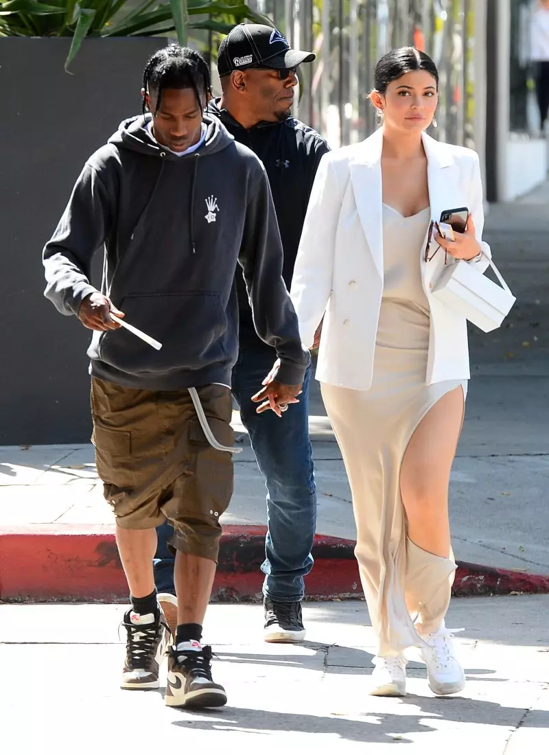 Kylie Jenner tan dress jaket putih sepatu tenis Travis Scott hoodie hitam celana pendek coklat berpegangan tangan