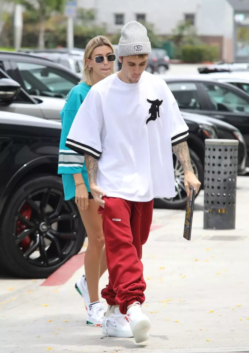 Justin Bieber ati Hailey Baldwin di ọwọ mu awọn ẹja yanyan ọsan mu jersey pupa sokoto funfun seeti ti o tobijulo aṣọ igbona igbeyawo