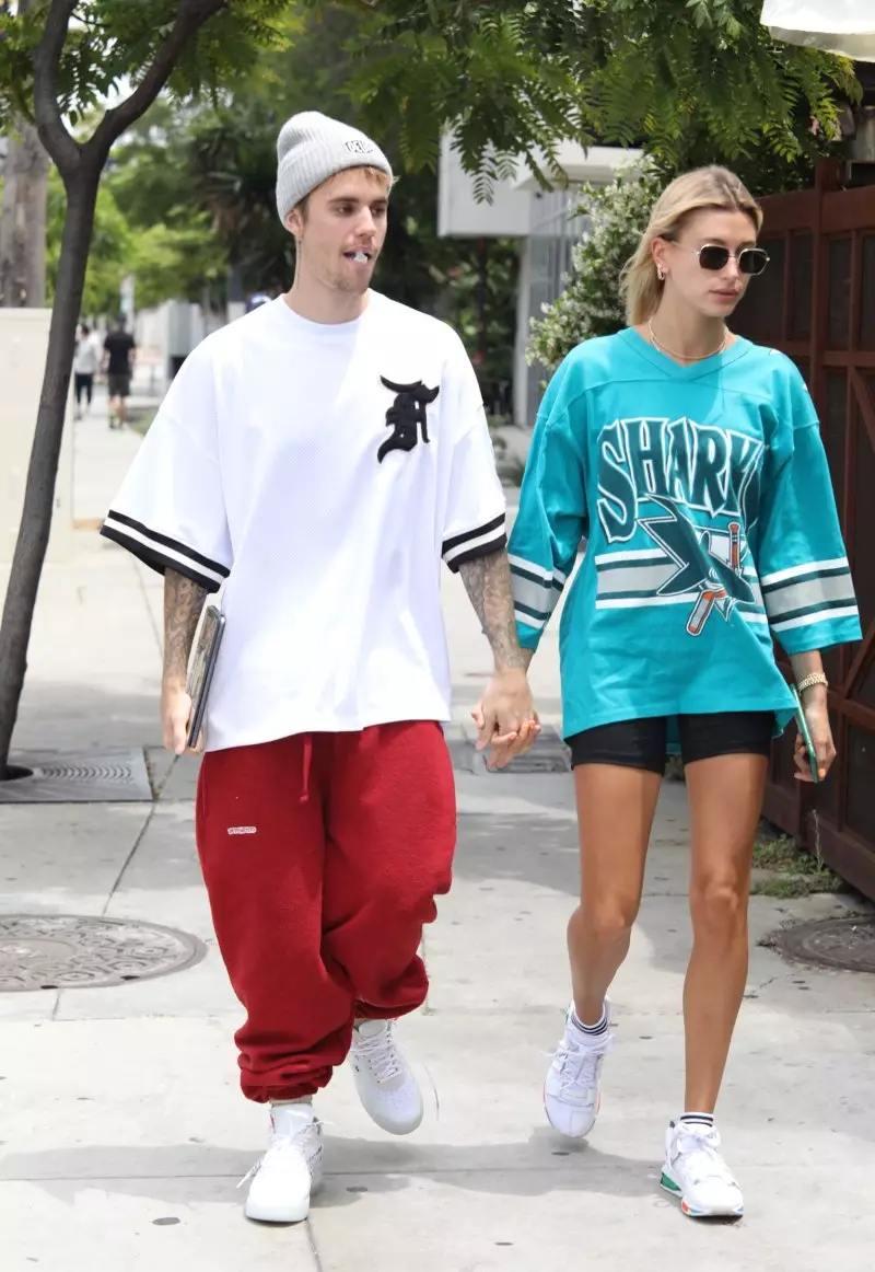 Justin Bieber ati Hailey Baldwin di ọwọ mu awọn ẹja yanyan ọsan mu jersey pupa sokoto funfun seeti ti o tobijulo aṣọ igbona igbeyawo