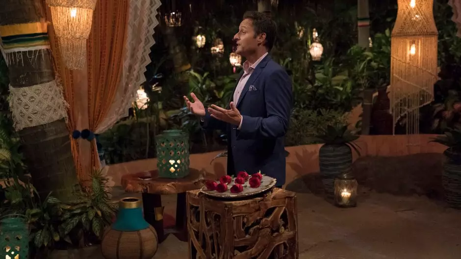 Bachelor-isäntä Chris Harrison seisoo Bachelor in Paradise -ruususeremoniassa sinisessä puvussa ja vaaleanpunaisessa paidassa ennen ruususeremoniaa