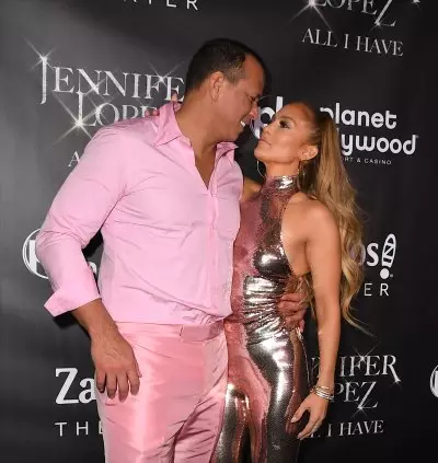 Дженнифер Лопес в серебряном блестящем комбинезоне с лямкой на шее и с любовью смотрит на Алекса Родригеса в розовой рубашке на пуговицах и розовых брюках