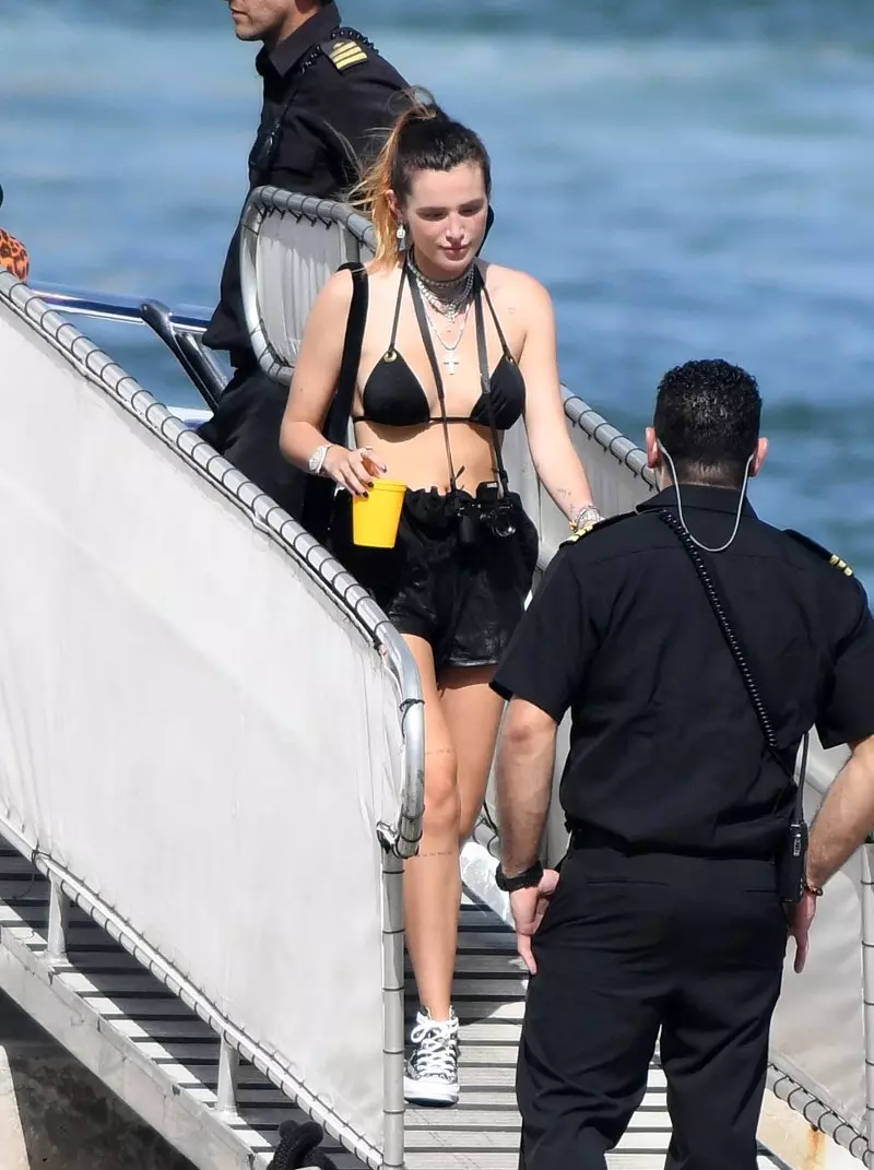 Bella Thorne yn in swarte bikinitop en swarte shorts dy't in drankje hâlde