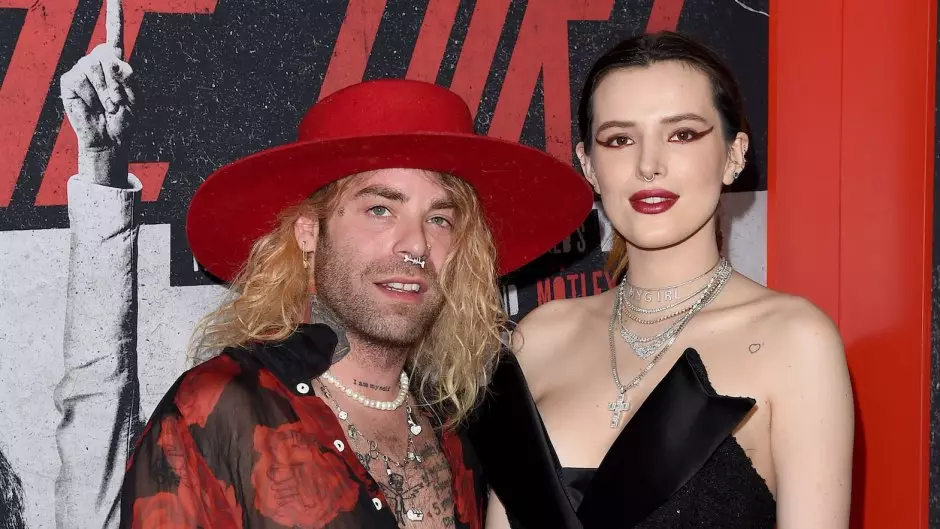 Mod Sun í rauðum hatti og Bella Thorne í svörtum ólarlausum kjól sitja fyrir á rauðu teppinu gift brúðkaupsathöfn