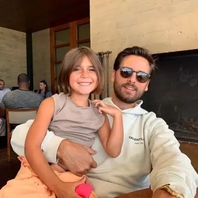 Penelope Disick သည် Scott Disicks ရင်ခွင်ပေါ်တွင်ထိုင်ပြီး ပြုံးနေပါသည်။