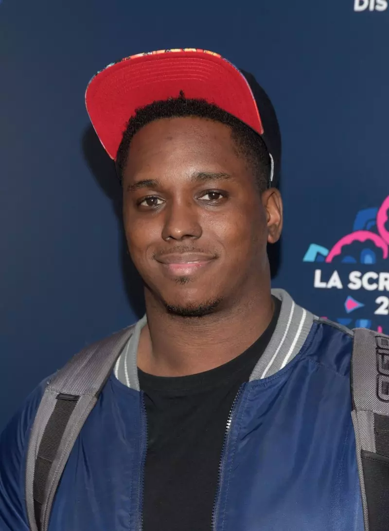 Kevin Barnett souriant portant un chapeau rouge et une veste bleue