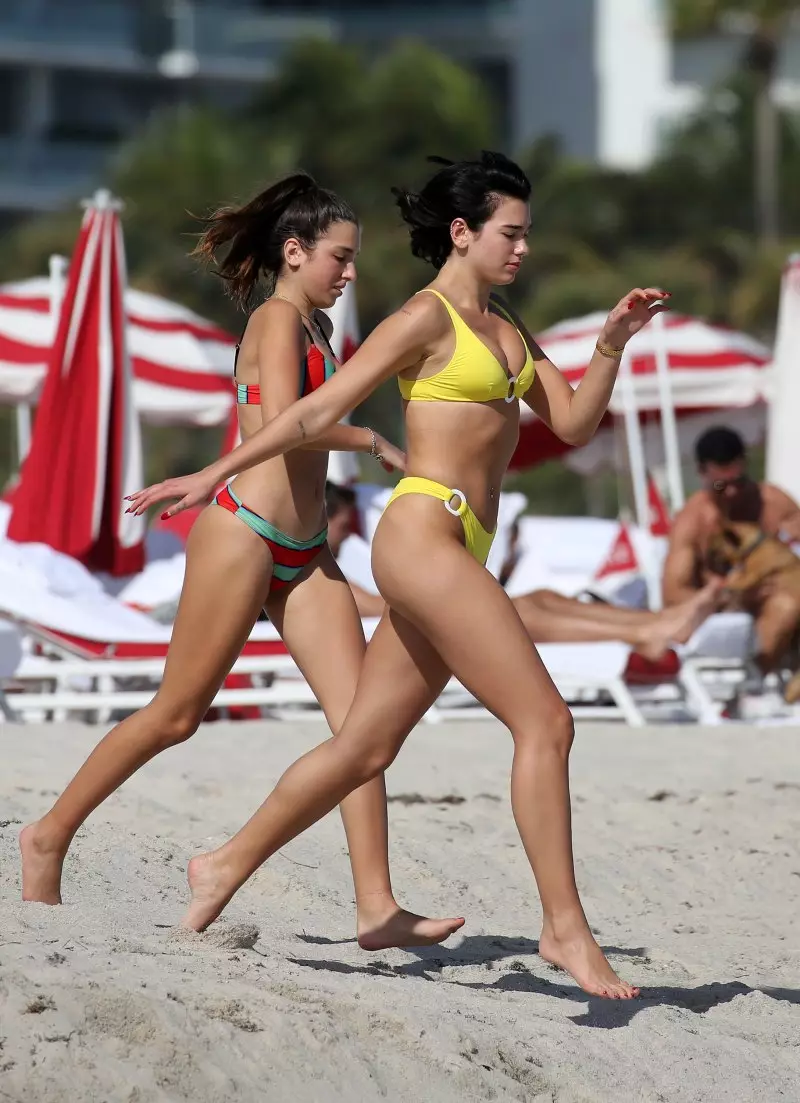 EKSKLUZĪVS: dziedātāja Dua Lipa valkā dzeltenu bikini, kad viņa kopā ar māsu Maiami peld okeānā un pēc tam sveicina savu draugu smiltīs.