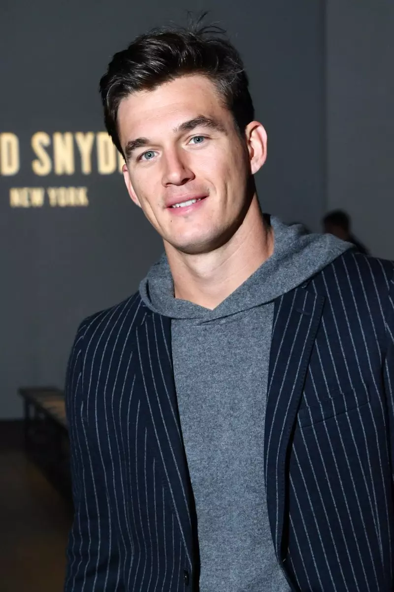 Tyler Cameron leva unha sudadera gris con un blazer de rayas azul na parte superior