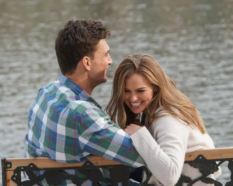 Bachelorette Tyler Cameron draacht in plaid shirt en sit op in bankje mei Hannah Brown te laitsjen